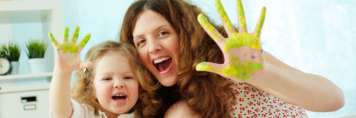 Eine Frau und ein Kind lachen und halten eine Hand hoch die voll mit Farbe ist 
